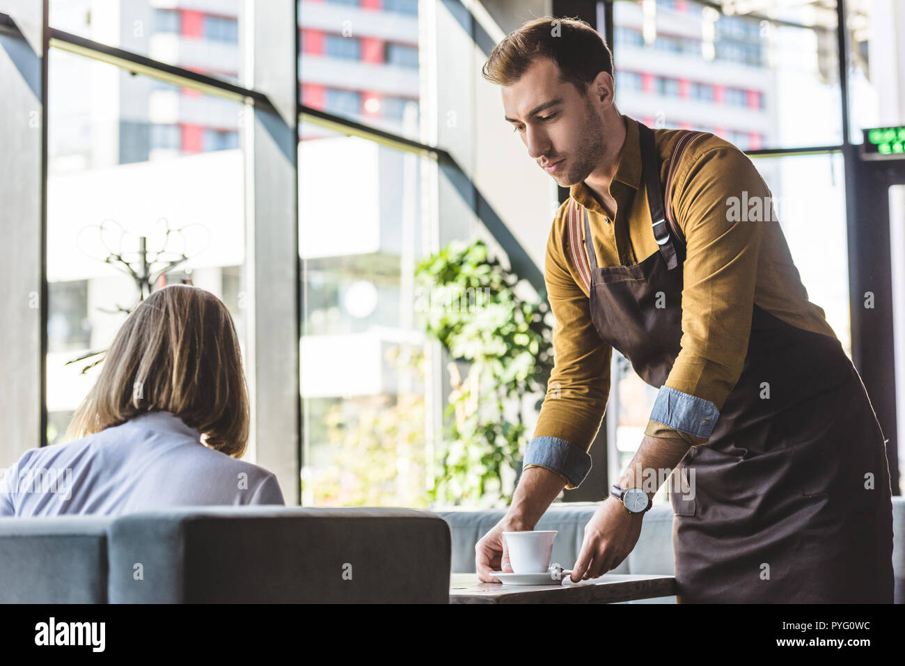 confident young waiter serving cup of coffee for female client at cafe ...