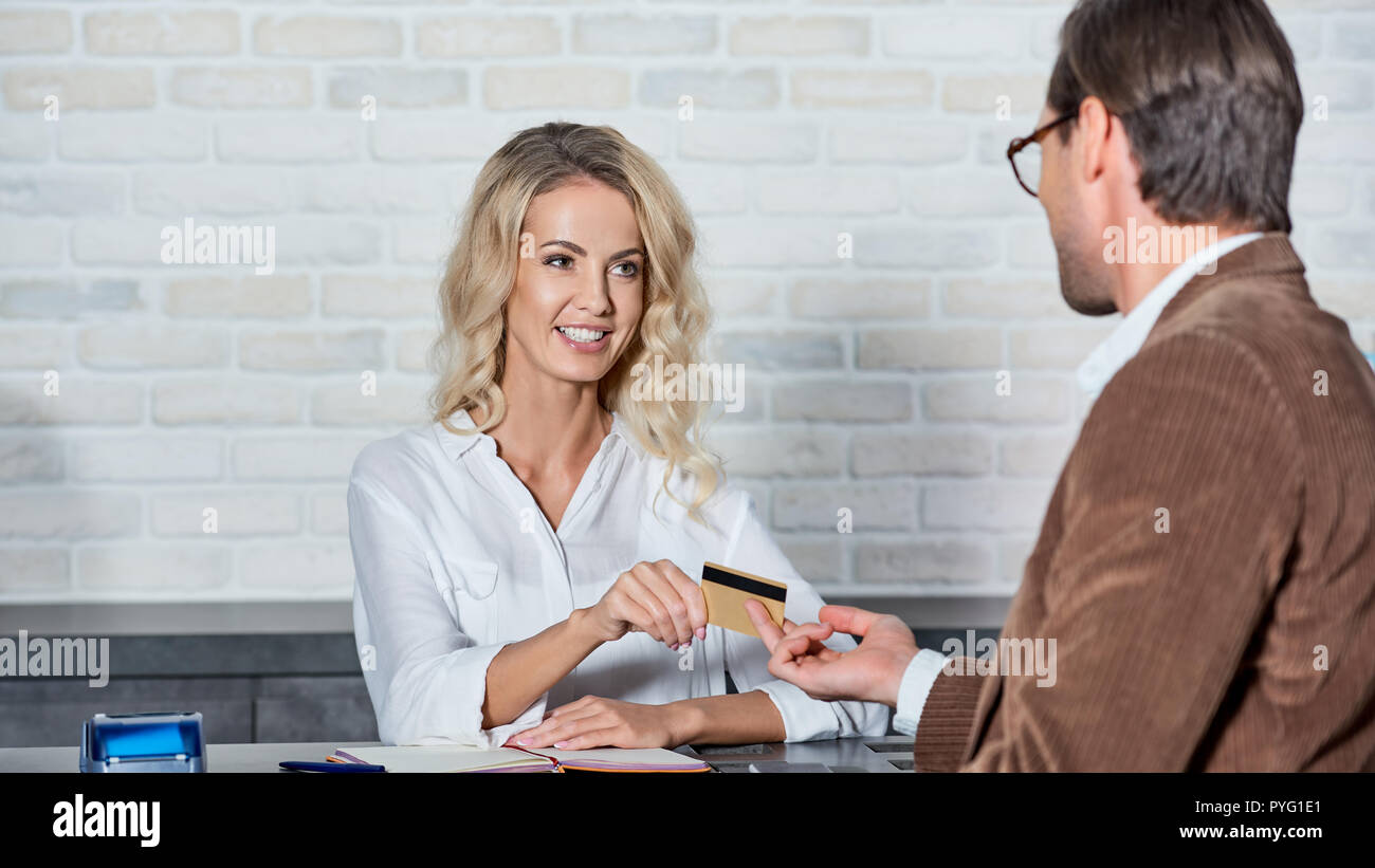 customer giving credit card to smiling young seller in shop Stock Photo ...