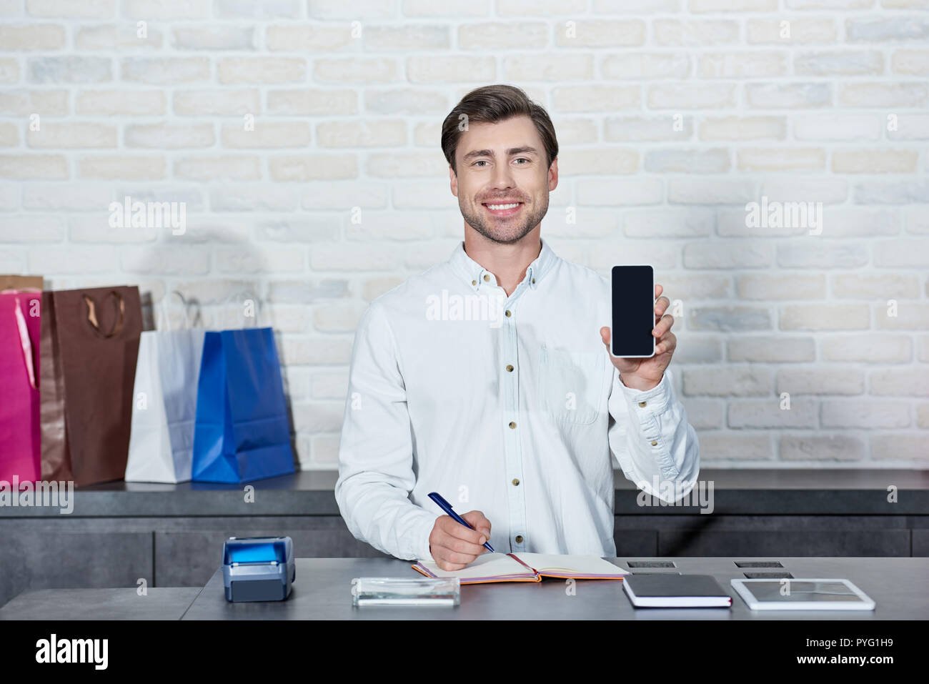 handsome young salesman holding smartphone with blank screen and ...