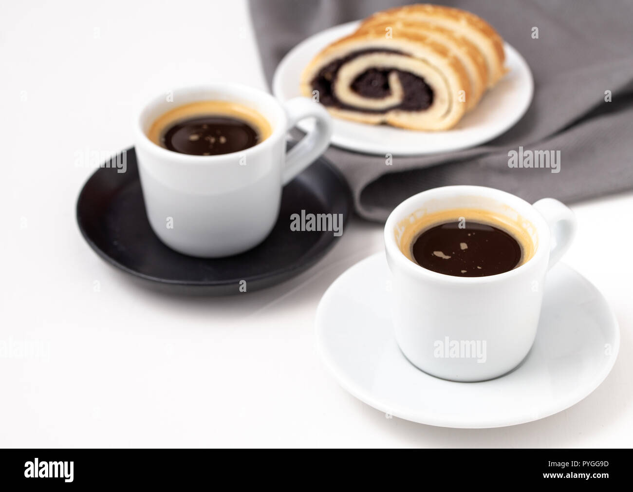 White cups of coffee on black saucer pad with poppy seed cake in behind ...