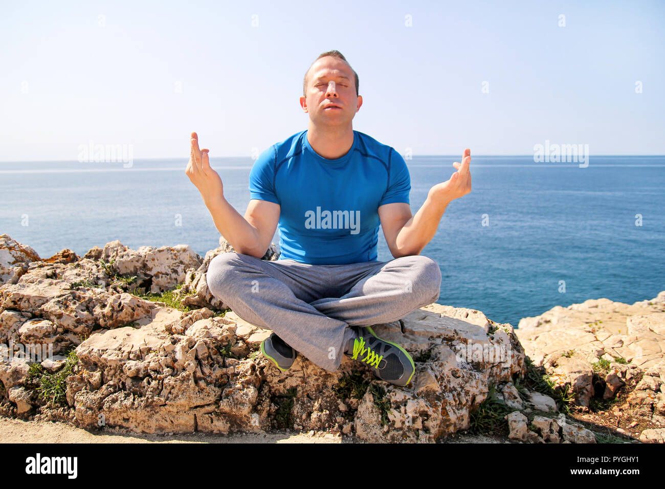 A fit man in the Lotus position on a seashore. Young fitness man doing ...
