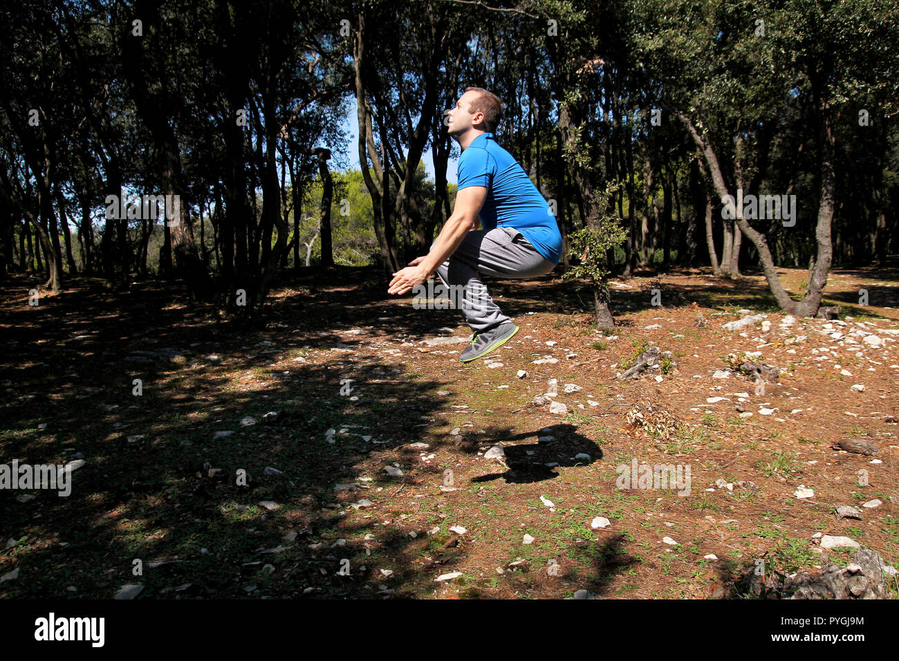Muscular man doing workout jump up in air exercise in forest. Handsome ...