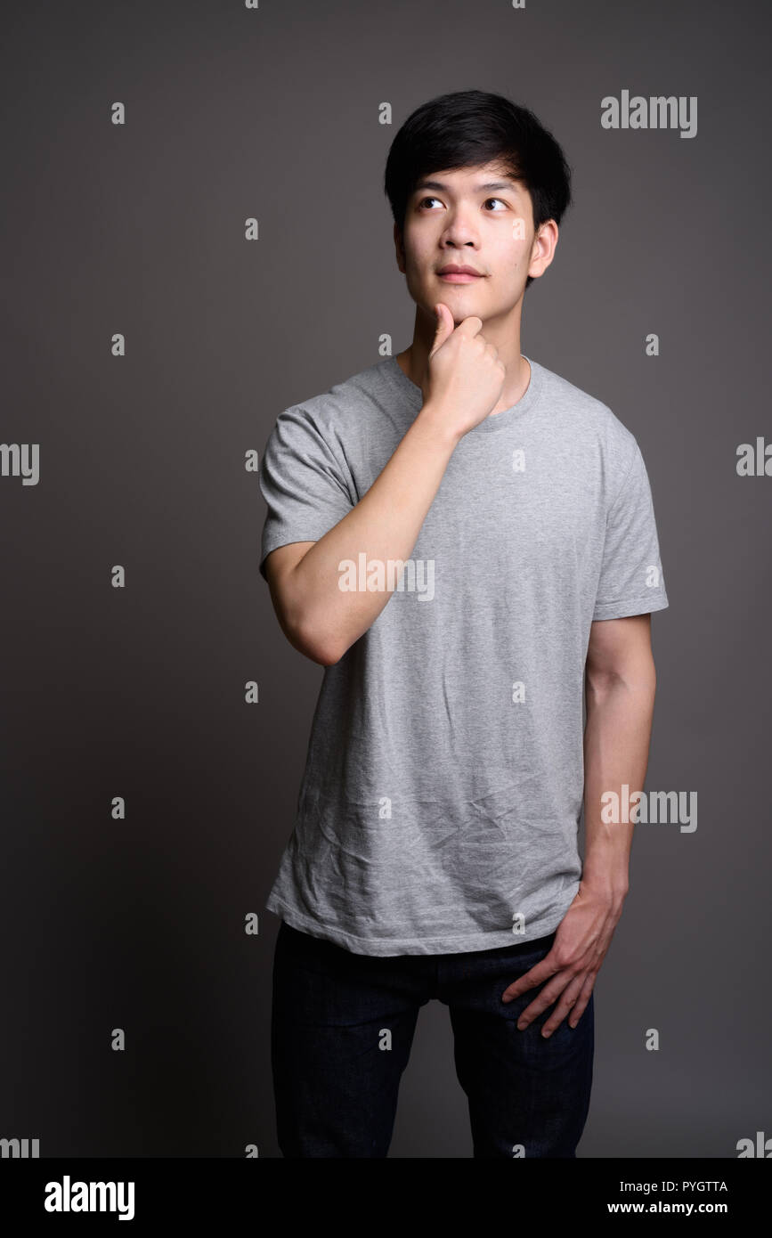 Young handsome Asian man thinking against gray background Stock Photo ...