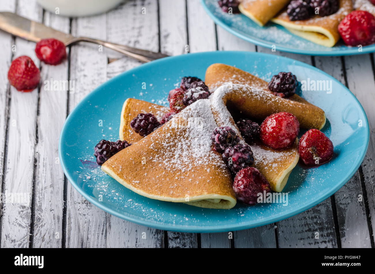 Homemade crepes with frozen berries, topped sugar, rustic wood board ...