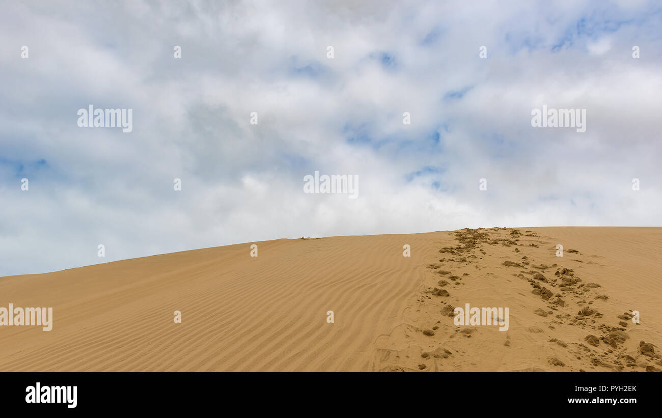 Ridge line of giant sand dunes against the sky with thick white clouds ...