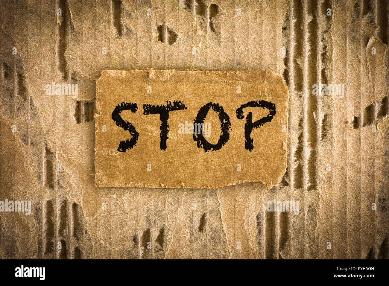 Piece of cardboard with word Stop on tattered corrugated cardboard ...