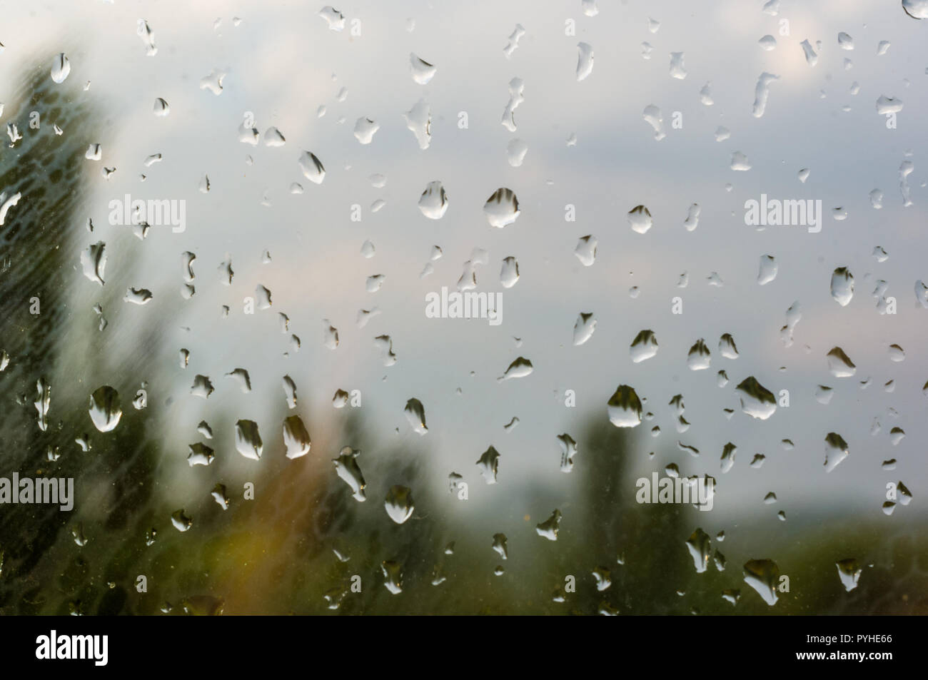 raindrops on window glass on background of cloudy sky and landscape ...