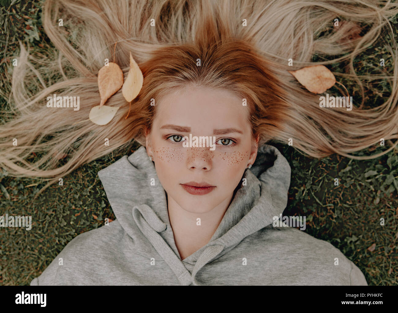 Young woman with freckles on her face laying in the park, leafs on her ...