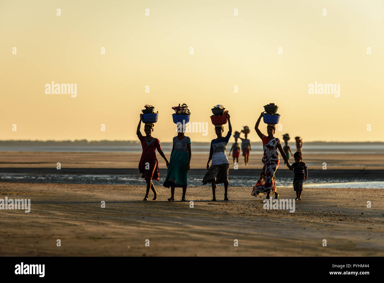 Black silhouette of women carrying catch on their heads walking along ...
