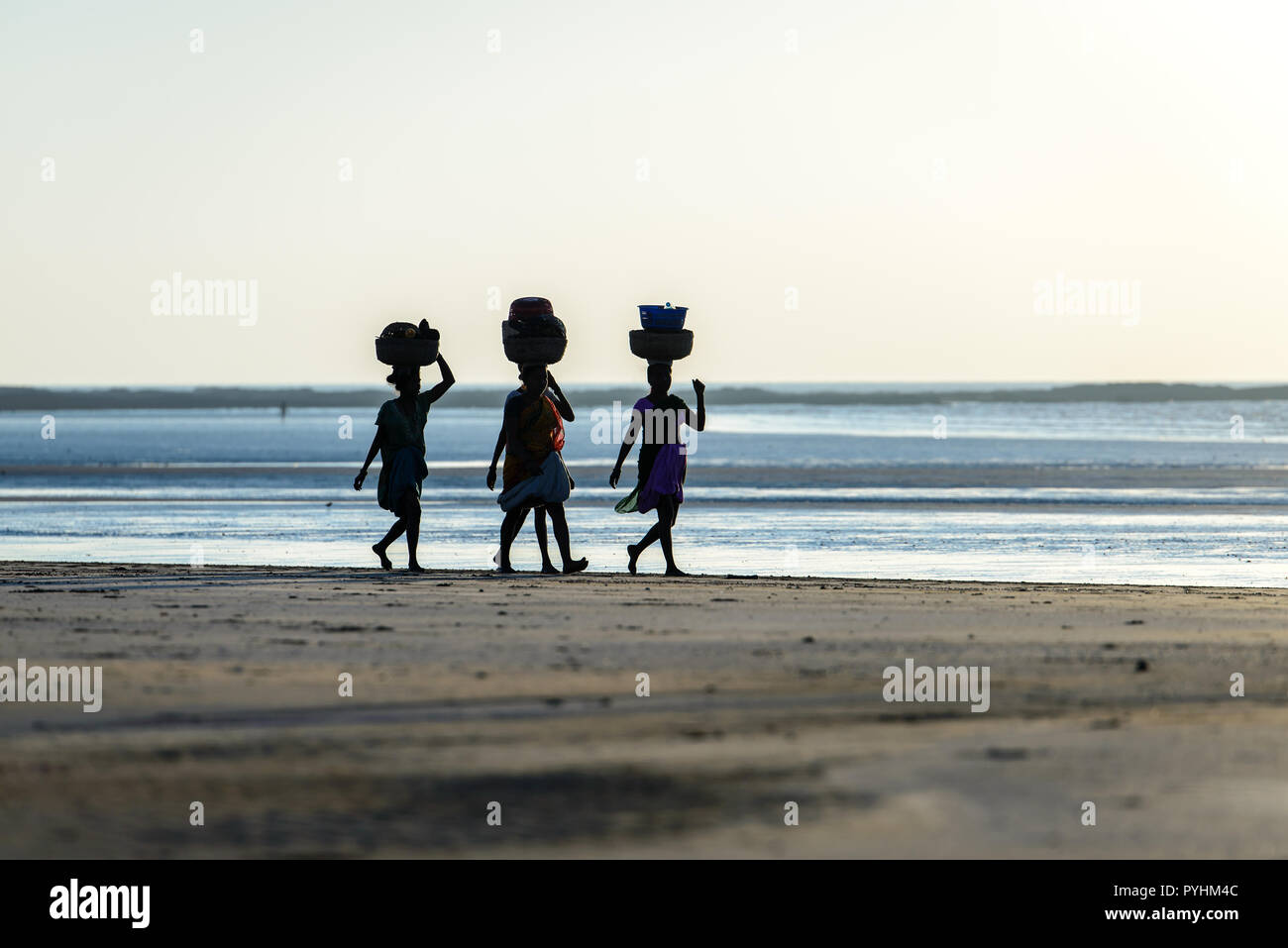Black silhouette of women carrying catch on their heads walking along ...