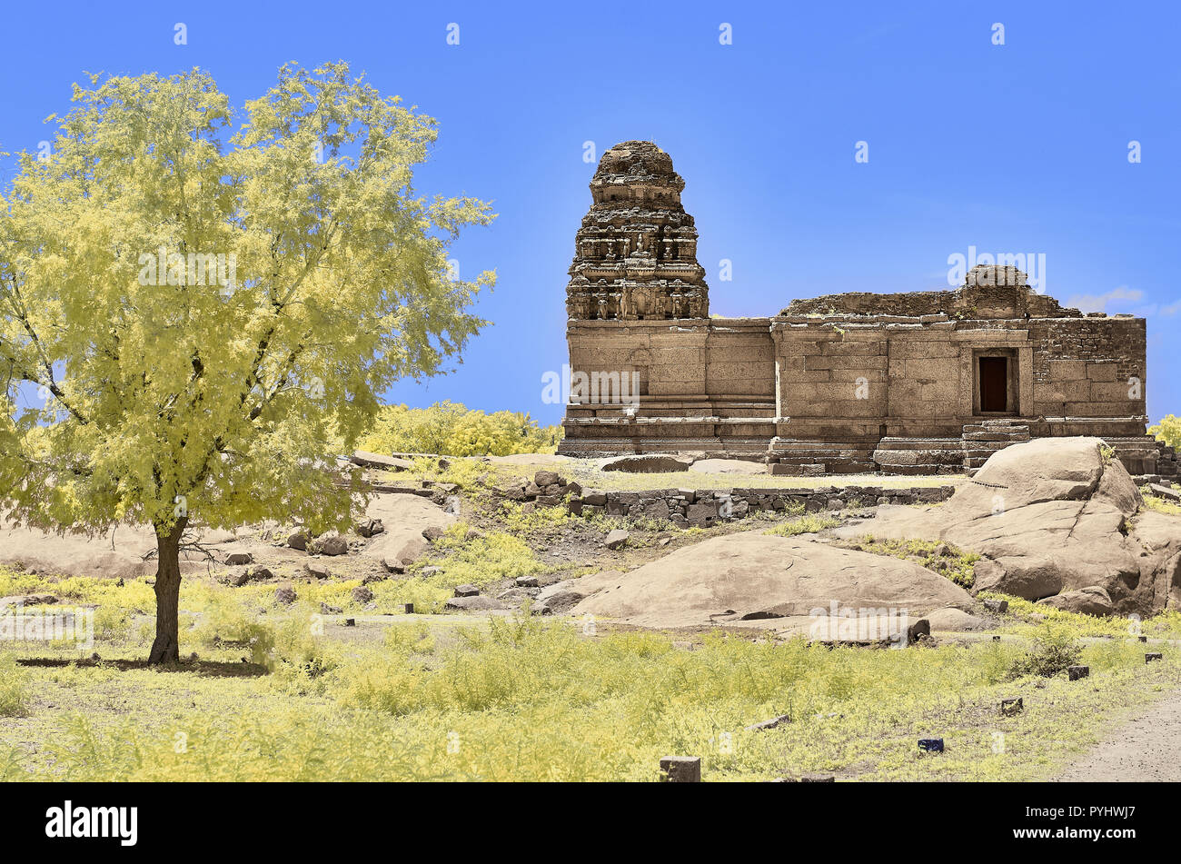 Temple in ruins under a blue sky with a tree and boulders in the ...