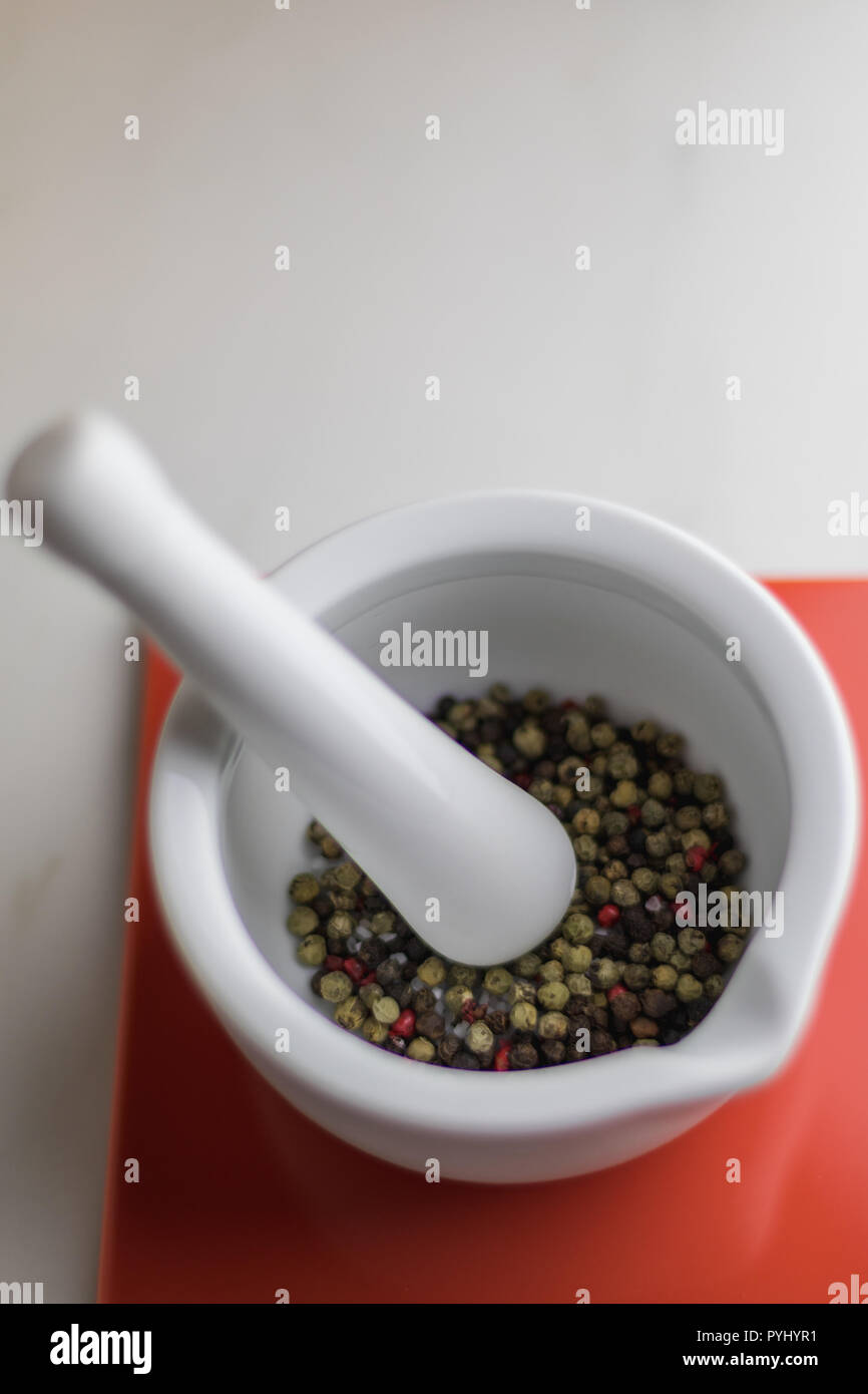 white mortar with colorful pepper inside on a red tile on a marble ...