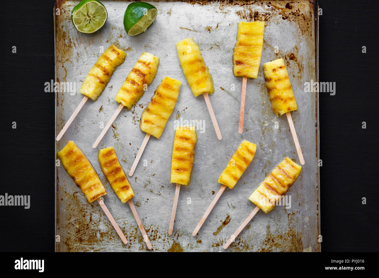 Grilled pineapple with lime on tray over black background, overhead ...