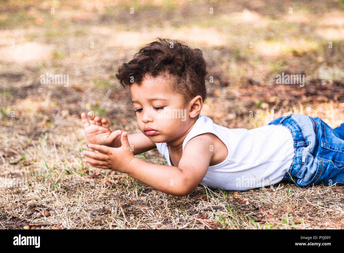Little boy laying on ground in park outdoor and playing with hands ...