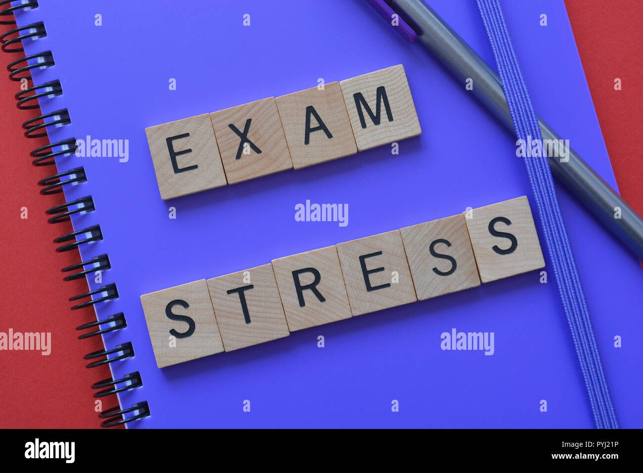 Purple spiral notebook and a pen, with the words Exams Stress in wooden ...