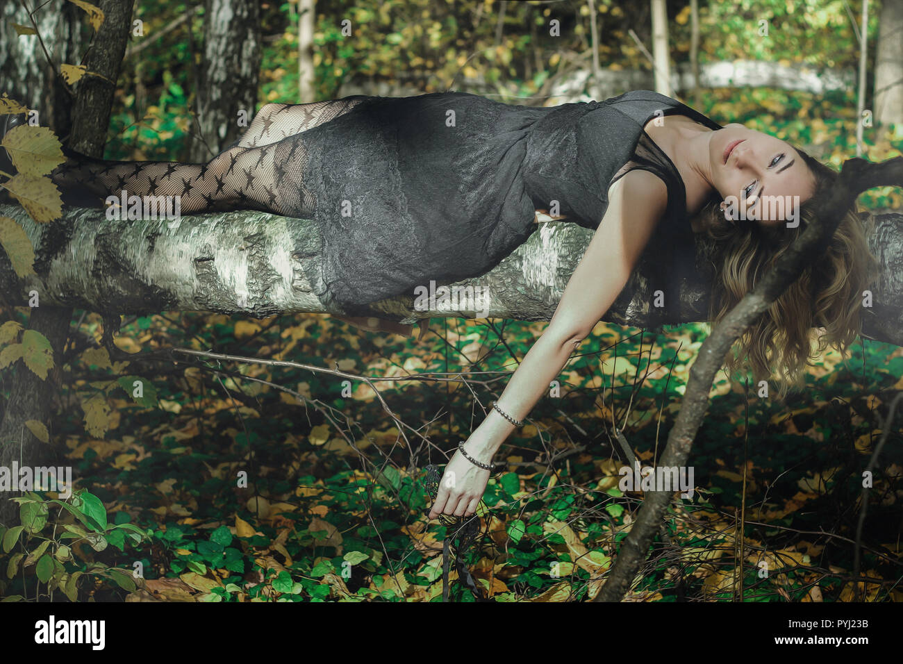 A young kind witch in a black dress with a black mask in a mystical ...