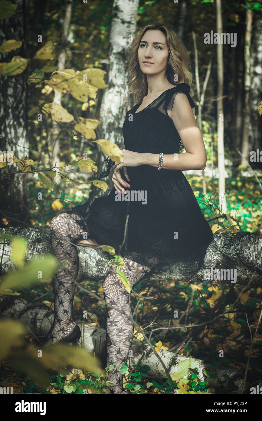 A young kind witch in a black dress with a black mask in a mystical ...