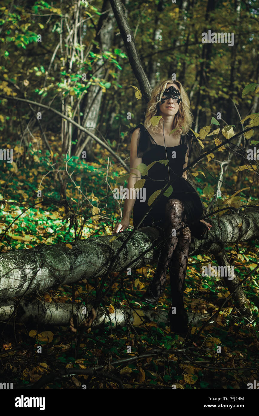 A young kind witch in a black dress with a black mask in a mystical ...