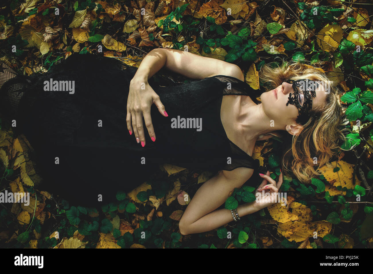 A young kind witch in a black dress with a black mask in a mystical ...