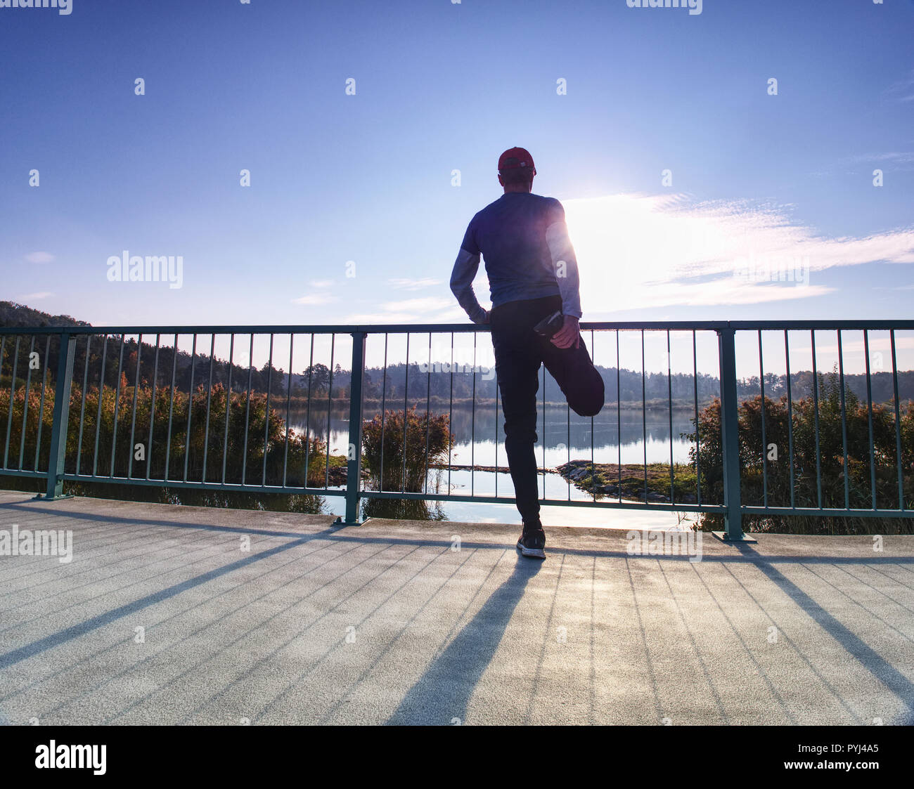 Runner doing stretching exercise on bay bridge. An active wiry man ...