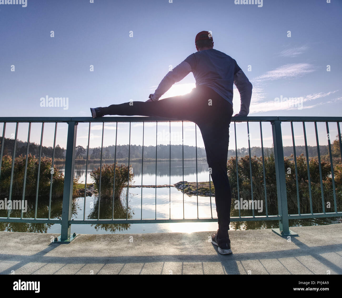 Man is stretching legs in break from run. The Sun is outlining man body ...