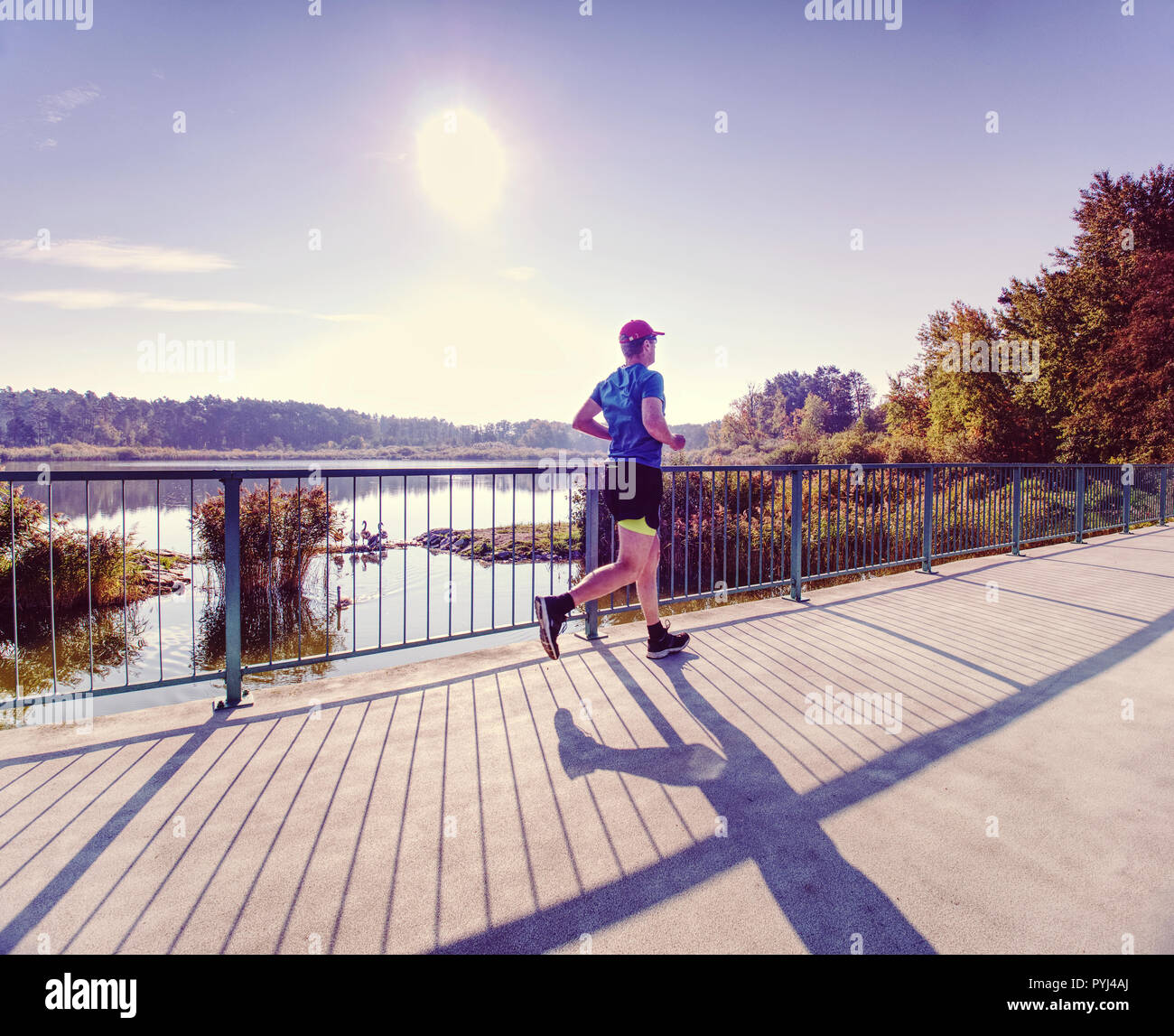 Full section view of fit slim man running on boardwalk. He is in sports ...