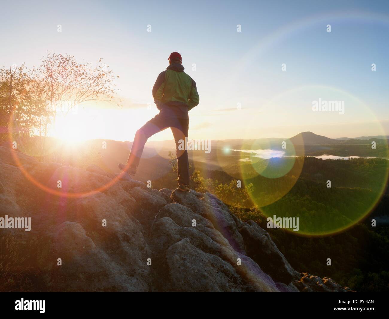 Sharp cliff edge with man watching over misty and foggy morning valley ...