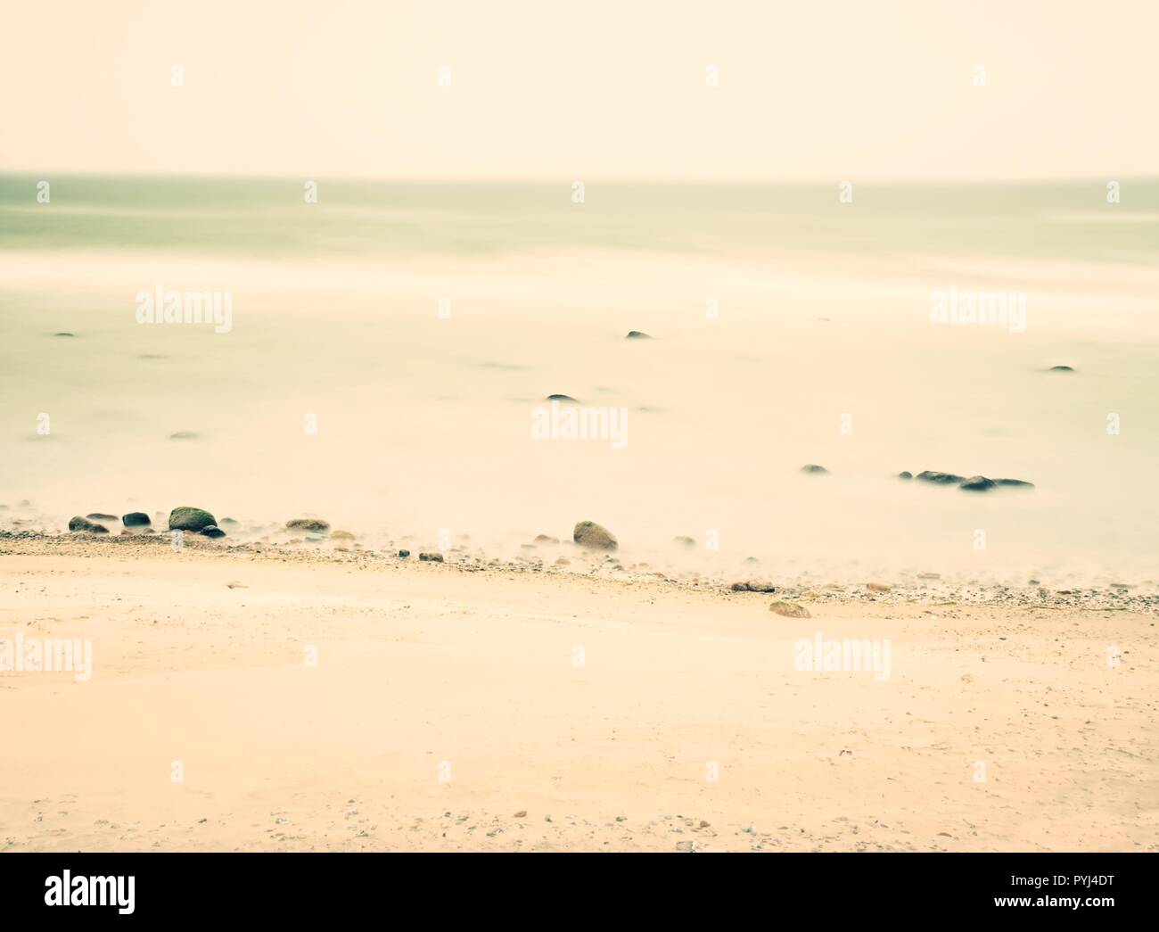 Stones and pebbles on sandy beach against foamy sea water. Low angle ...