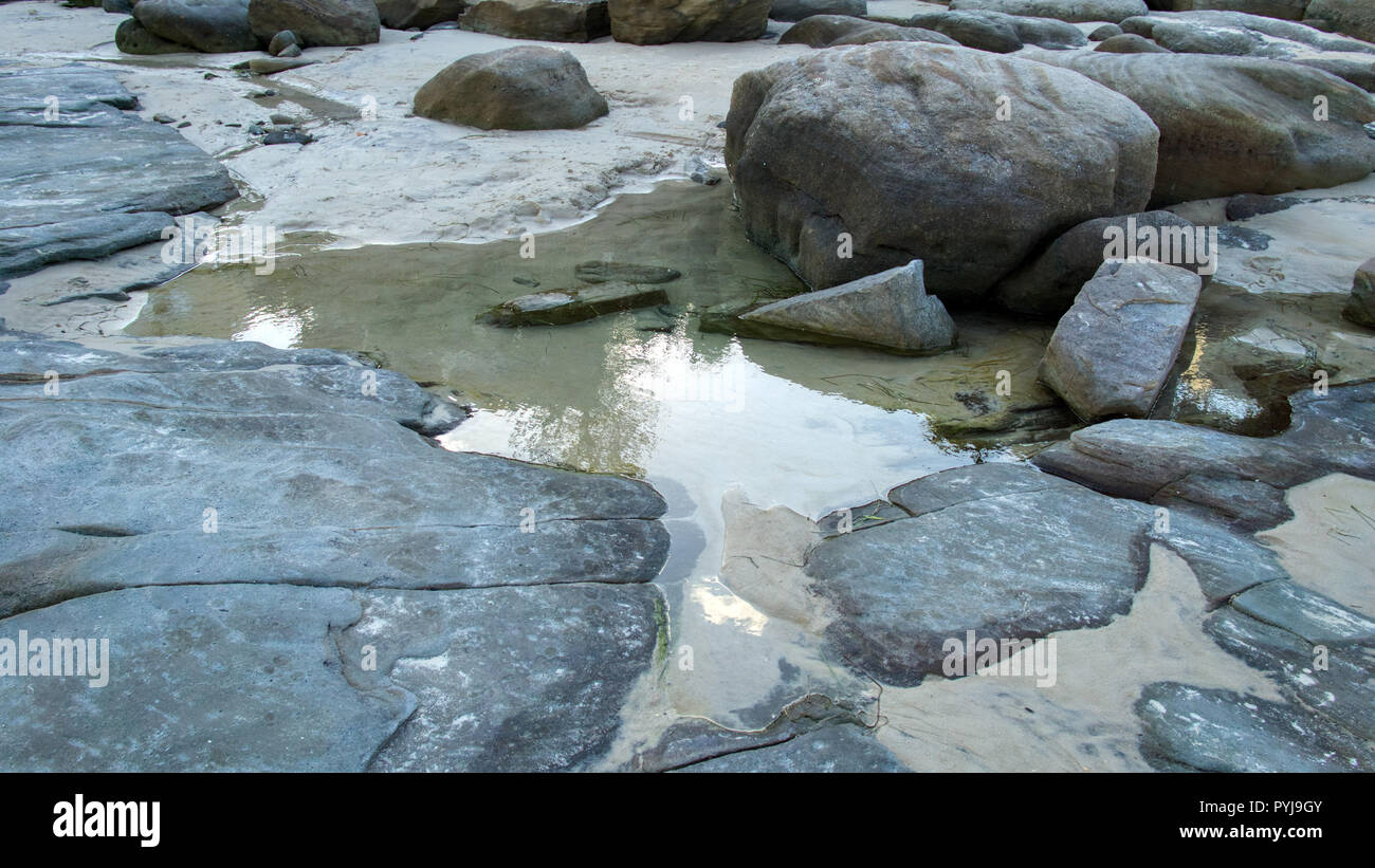 Large grey rocks and boulders in calm shallow sea water, wide image ...