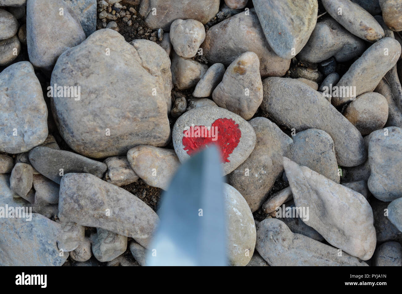 Cutting knife diving pink heart painted with lipstick on piece of stone ...