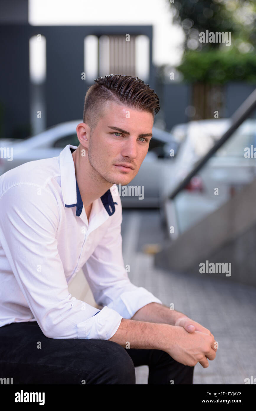 Young handsome man thinking while sitting outdoors Stock Photo - Alamy