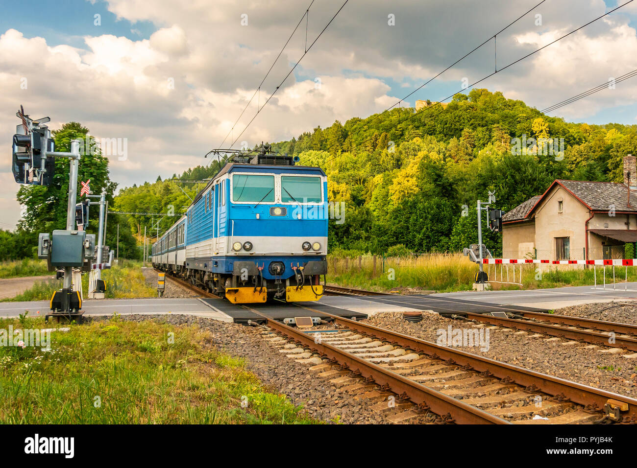 The blue electric train arriving at the crossing with the barriers. A ...