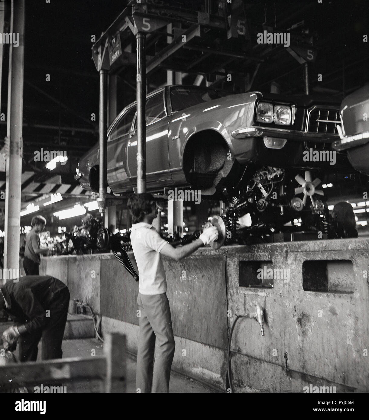 1970s, historical, a male car worker on an assembly line, with an ...