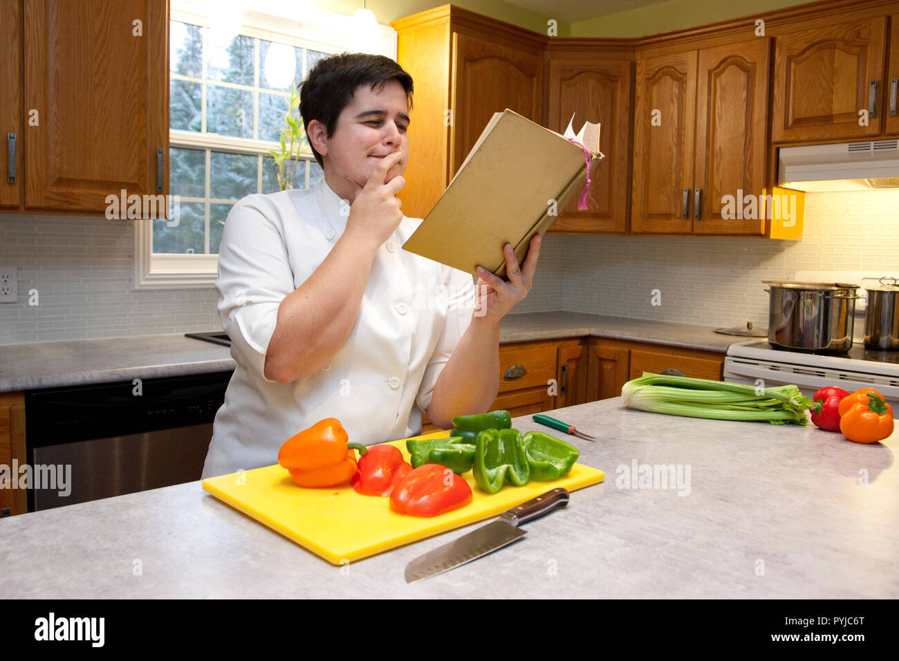 Person in their kitchen looking at a cookbook and considering a recipe ...