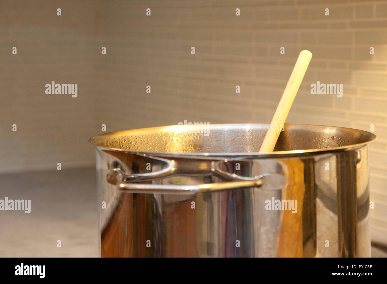 A large metal vat of soup or stew on the stove with a wooden handle in ...