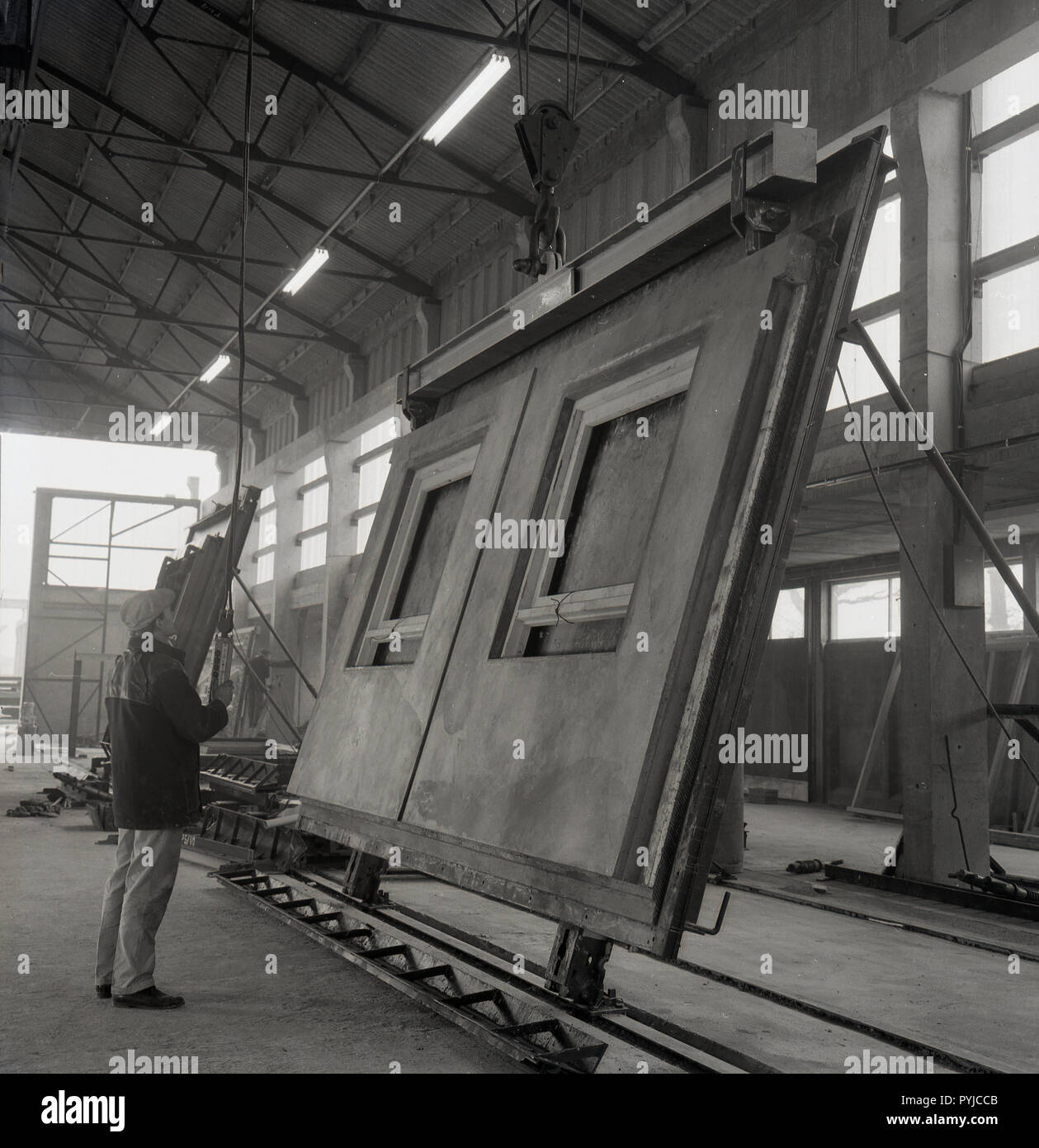 1960s, male worker in hanger using a pulley to put into place a large ...
