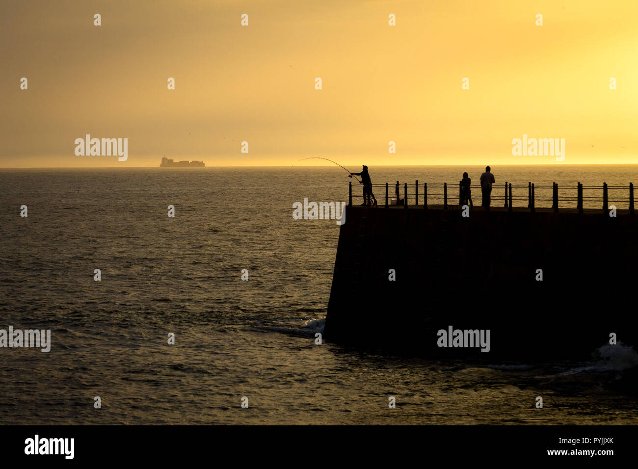 Two people and a fisherman stand on a silhouetted pier at sunset Stock ...