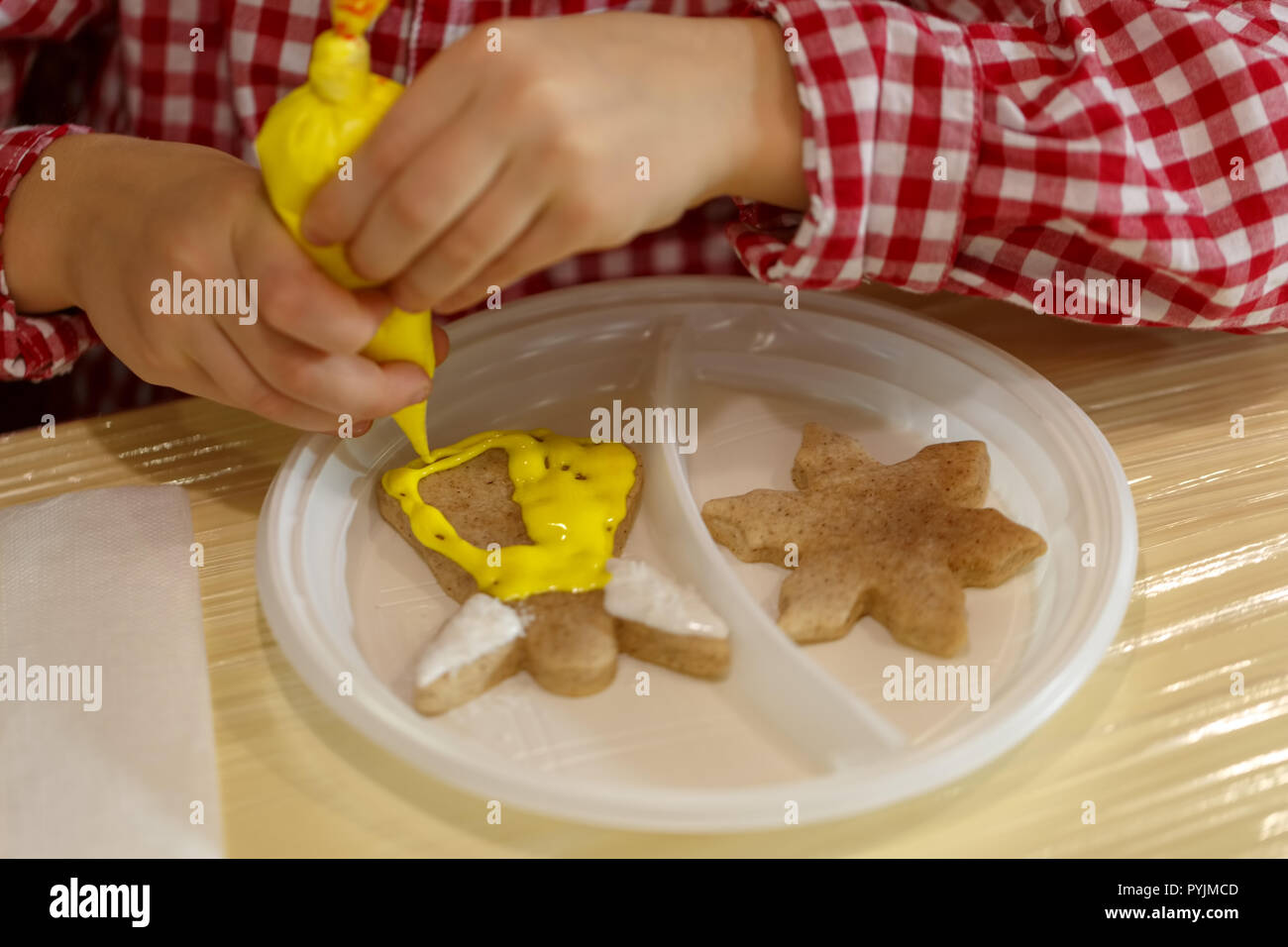 Boy in a plaid shirt is decorating with yellow cream the cookies in the ...