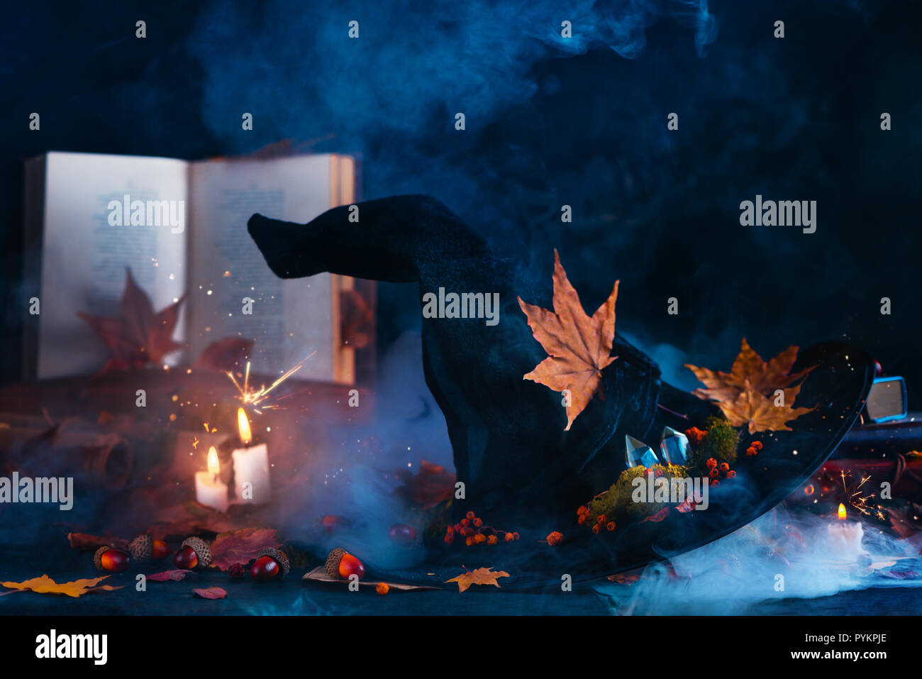 Witch hat in a spooky still life with candles, smoke and sparks. Occult ...