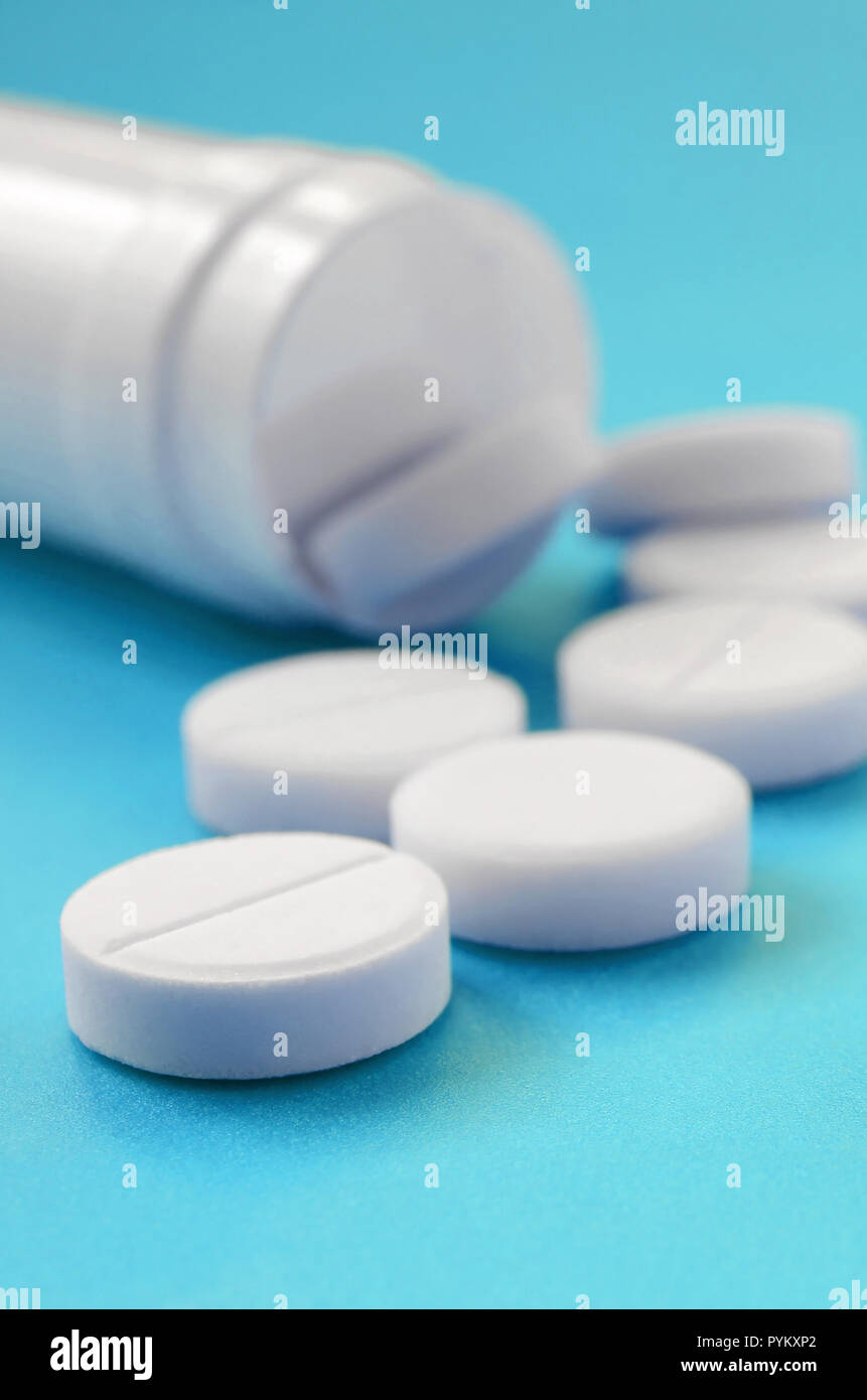 Several white tablets fall out of the plastic jar on the blue surface ...