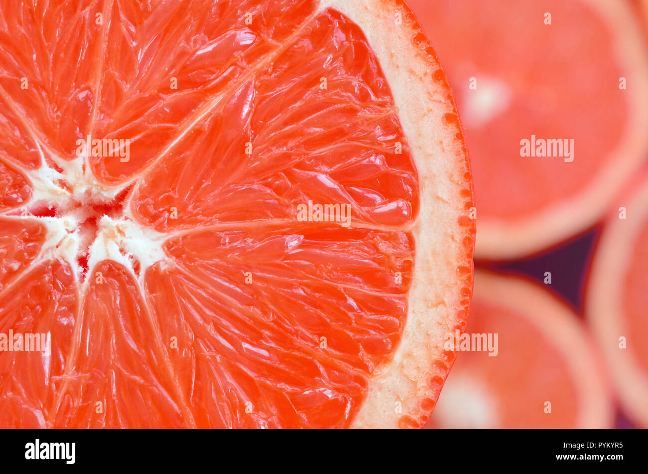 Top view of a fragment of the red grapefruit slice on the background of many blurred grapefruit ...