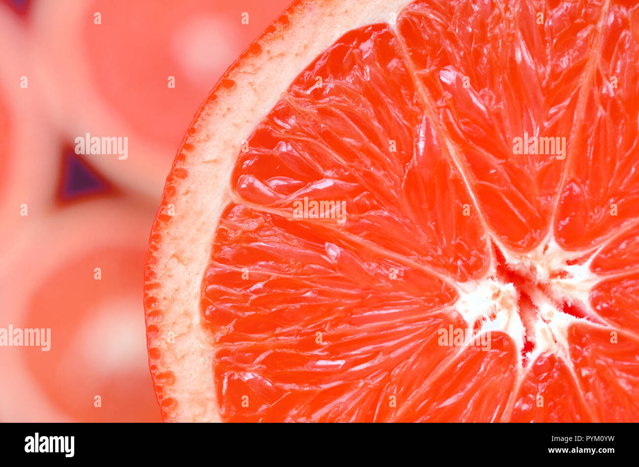 Top view of a fragment of the red grapefruit slice on the background of many blurred grapefruit ...