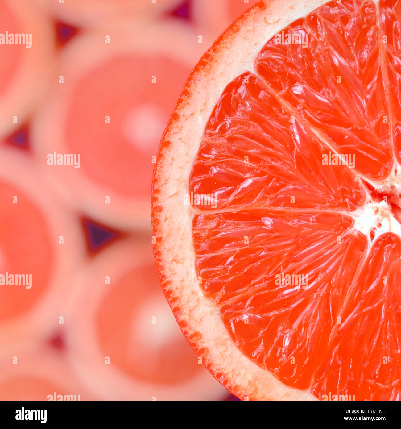 Top view of a fragment of the red grapefruit slice on the background of many blurred grapefruit ...