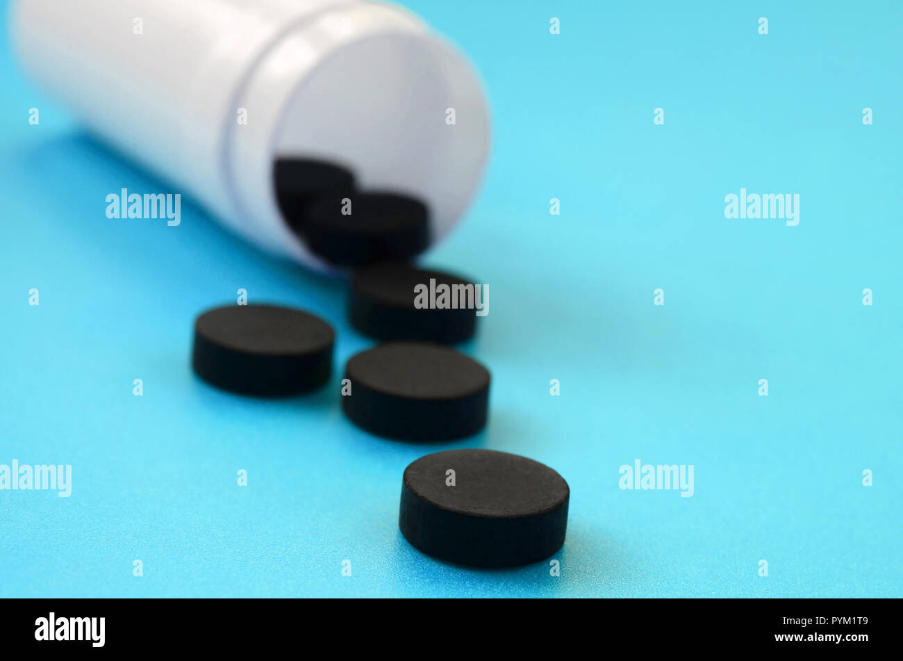 Several black tablets fall out of the plastic jar on the blue surface ...