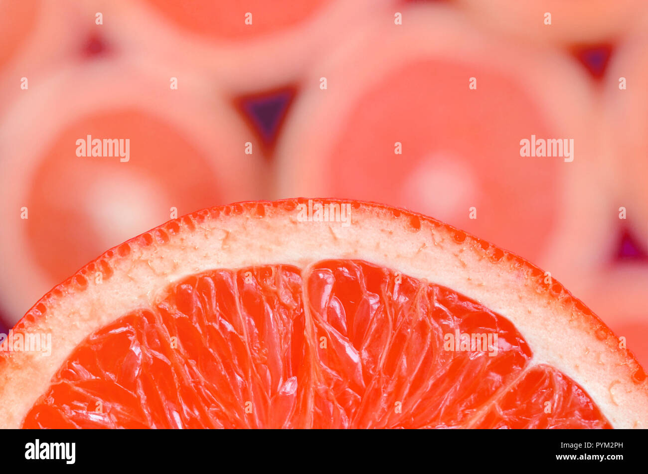 Top view of a fragment of the red grapefruit slice on the background of many blurred grapefruit ...
