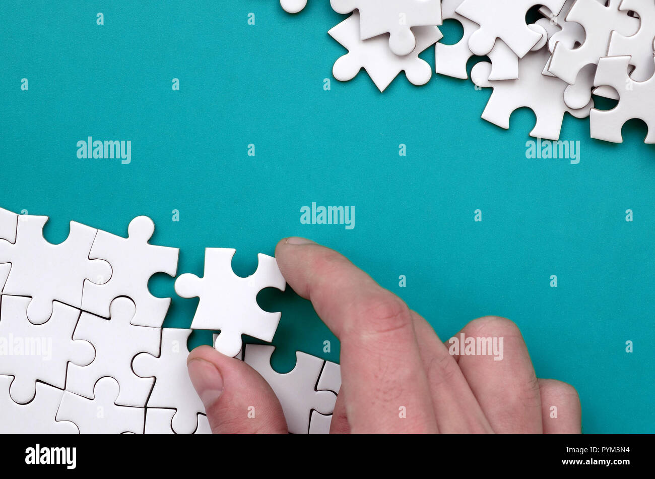 The hand folds a white jigsaw puzzle and a pile of uncombed puzzle ...