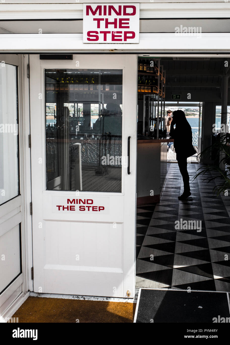 mind the step signs, silhouetted customer at bar. dark interior bright ...
