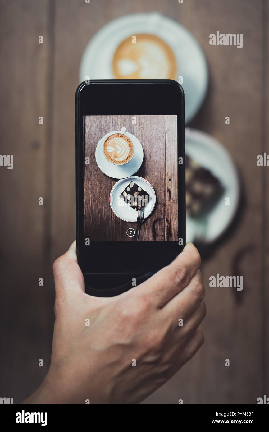 Top view of Hand holding mobile take a photo of coffee cup and cake on ...