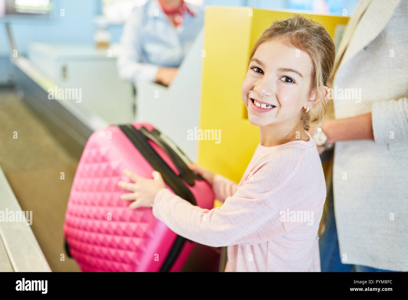 Little girl happily smiles at the check-in desk while bagging suitcase ...