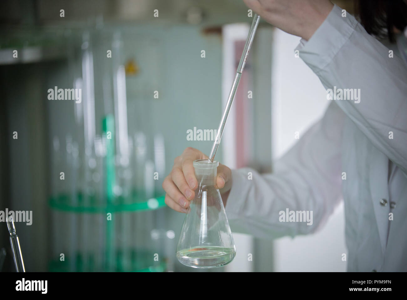 Chemical laboratory. Young woman holding a flask, dripping something ...